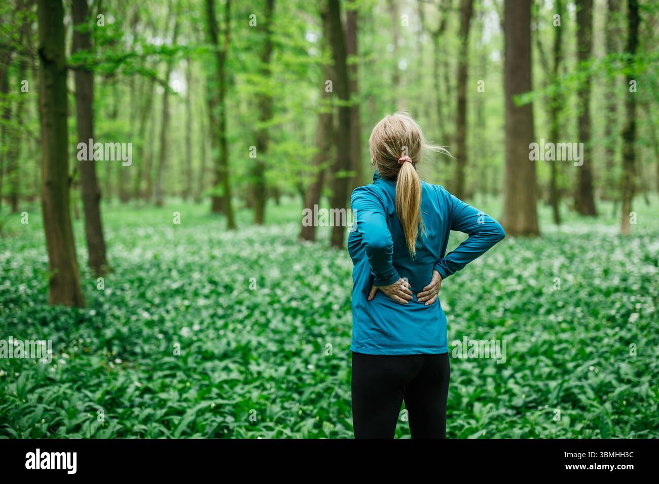 Woman feeling lower back pain while jogging in forest. Runner ...