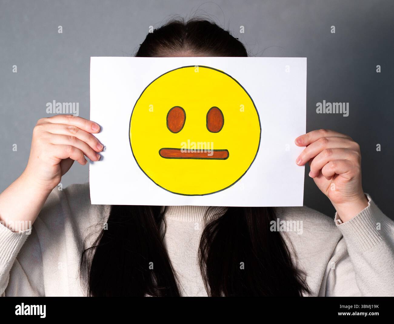 Woman holding emoji mask without smile and any expression in front of ...
