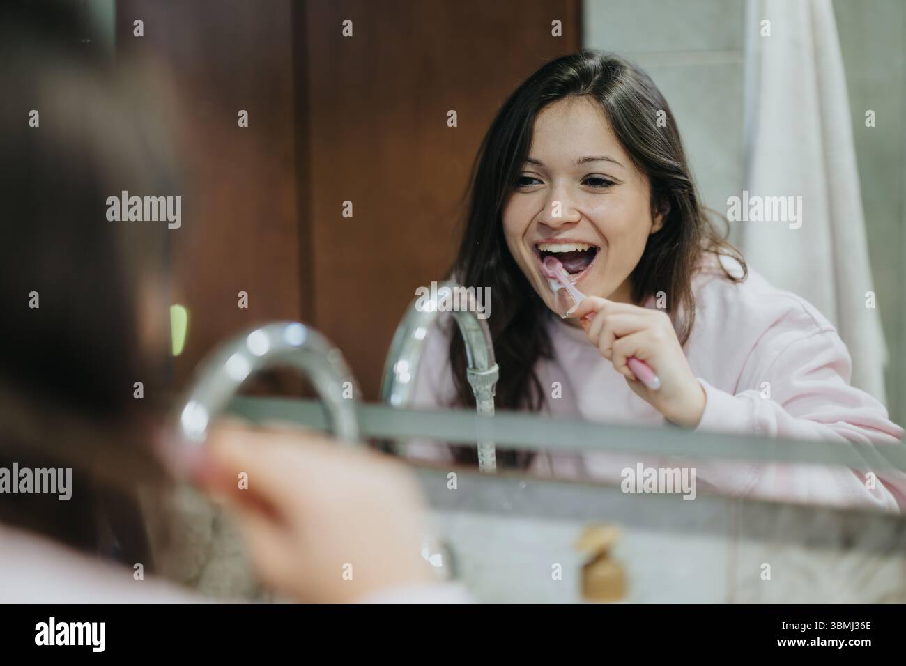 Woman smiling as she brushes her teeth in a bathroom mirror reflection Stock Photo - Alamy
