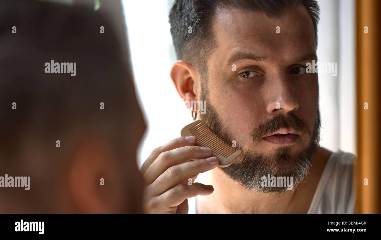 Clean-boy grooming. Man trims, styles his beard with focus and ...