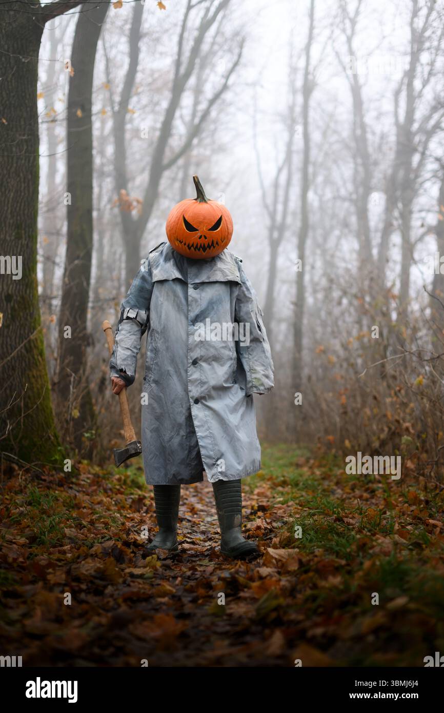 Scarecrow with axe in an old torn cloak and jack-o'-lantern pumpkin ...