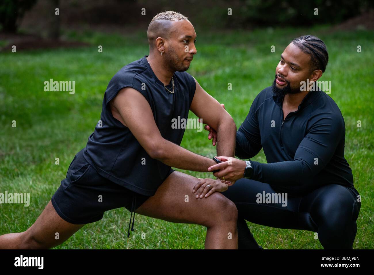 A personal trainer helping a client with a yoga pose outdoors Stock ...