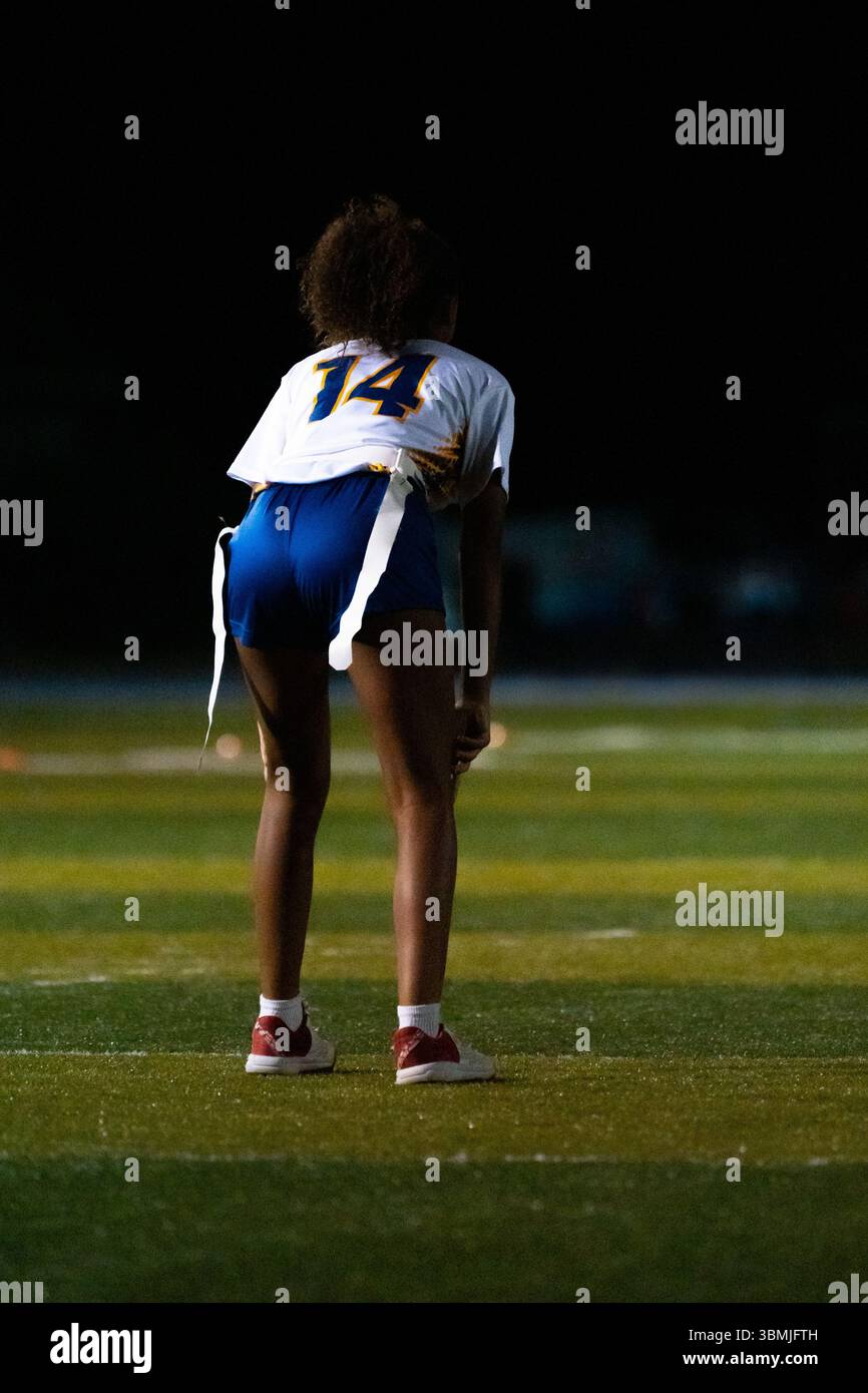 A female flag football player in ready stance under stadium lights ...