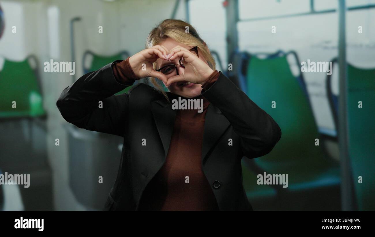 Woman smiling on a bus showing a heart gesture with her hands in a ...