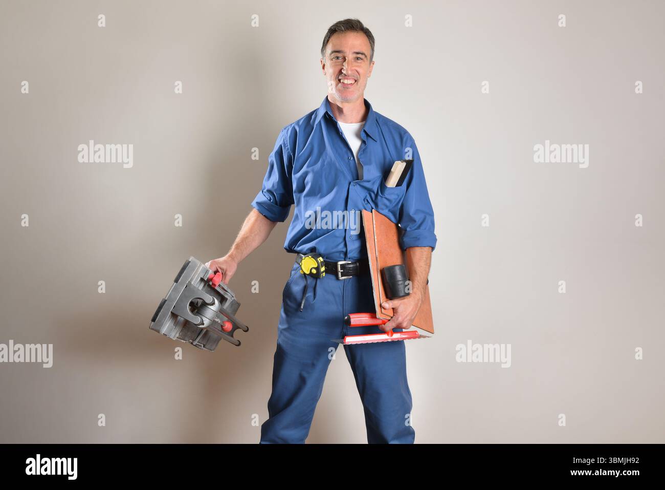 Tiler in work clothes smiling with ok gesture holding tools on isolated ...