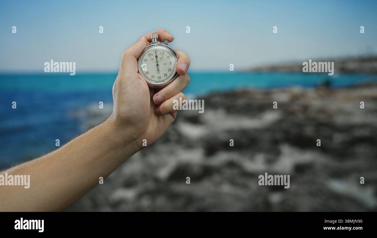 Man holding stopwatch on a scenic seaside beach with a clear blue sky ...