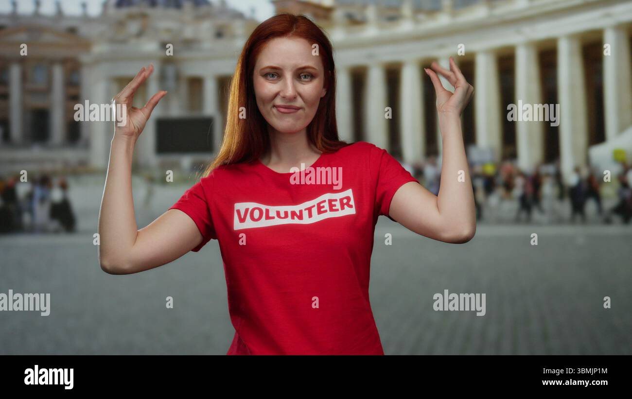 Redhead woman wearing a volunteer shirt stands in vatican city, engaging in conversation in the ...