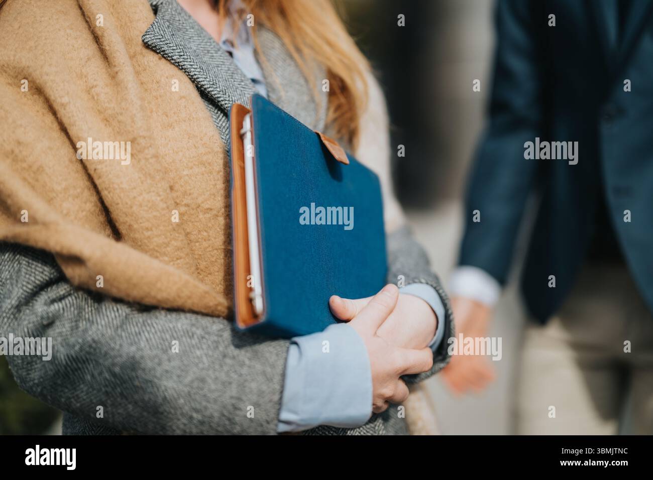 Person holding a folder while walking outdoors in professional attire ...