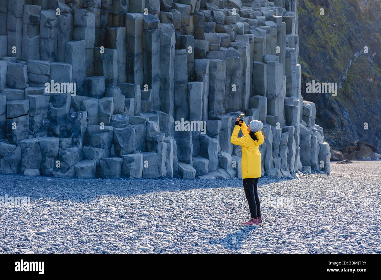 A traveler in a bright yellow jacket marvels at the towering basalt ...