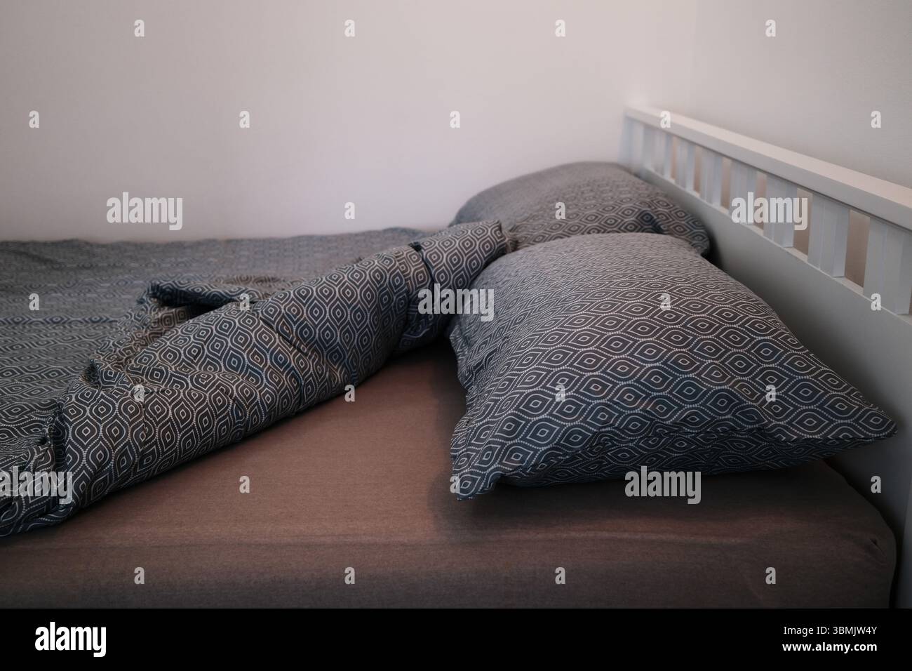 Crumpled patterned blanket and pillows on an unmade bed, capturing a ...