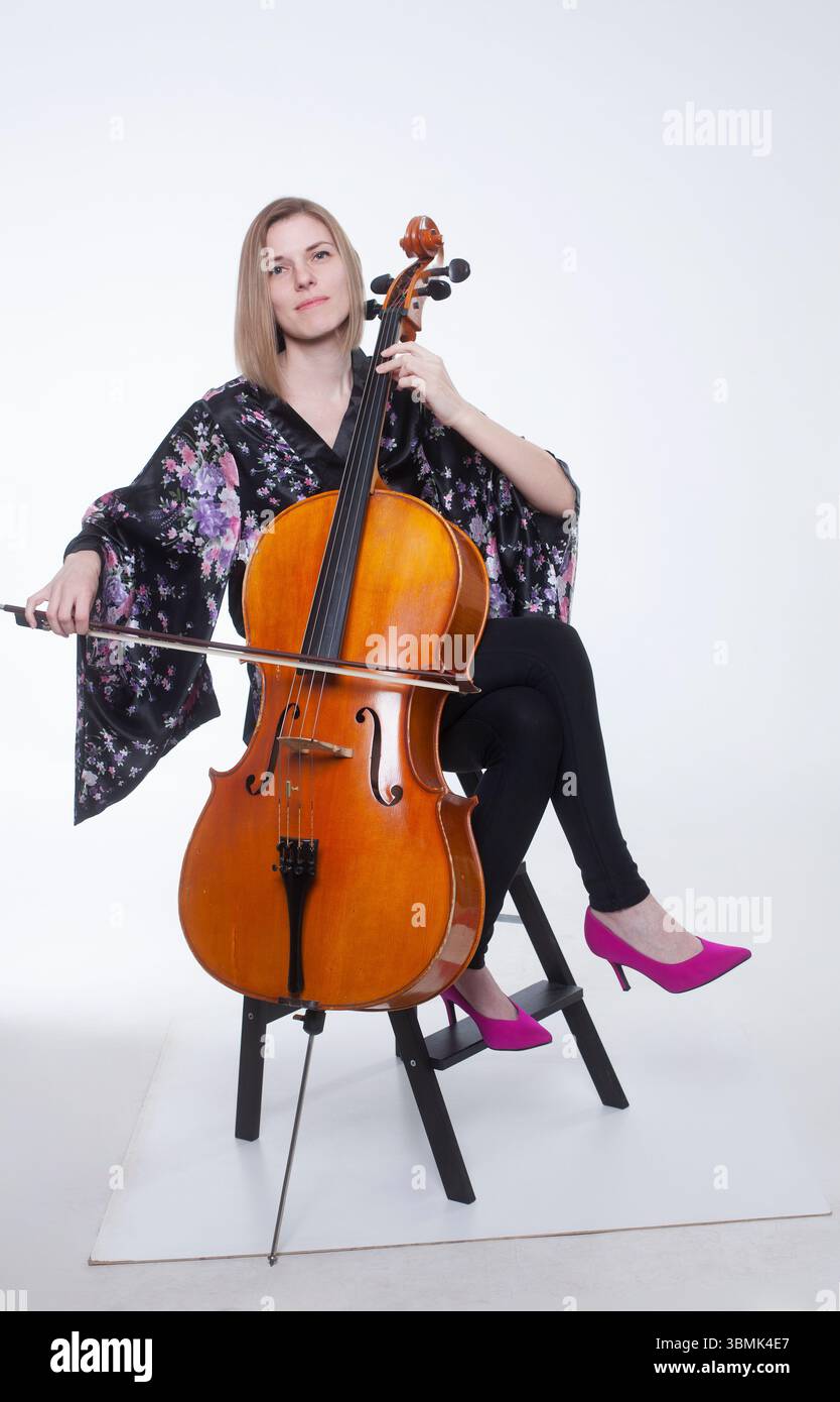 Caucasian woman in floral kimono robe plays cello in a studio setting ...