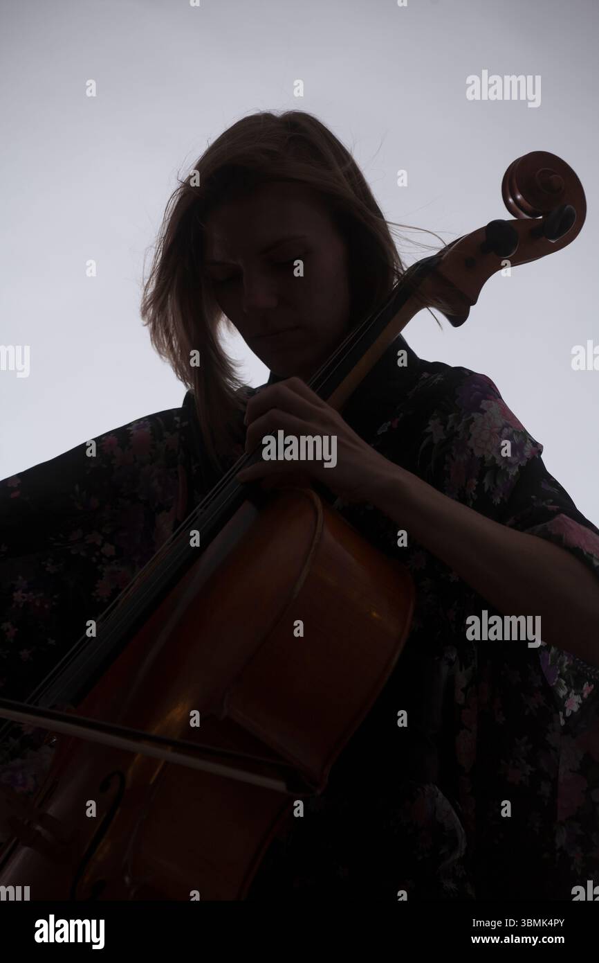 Young adult woman playing cello in studio, wearing dark floral top ...