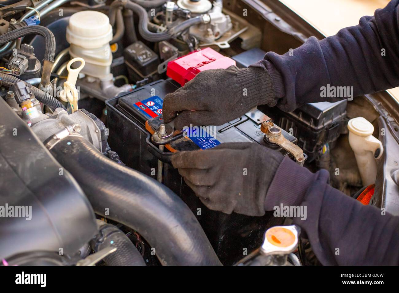 A man wearing gloves securely fastens a car battery terminal after ...