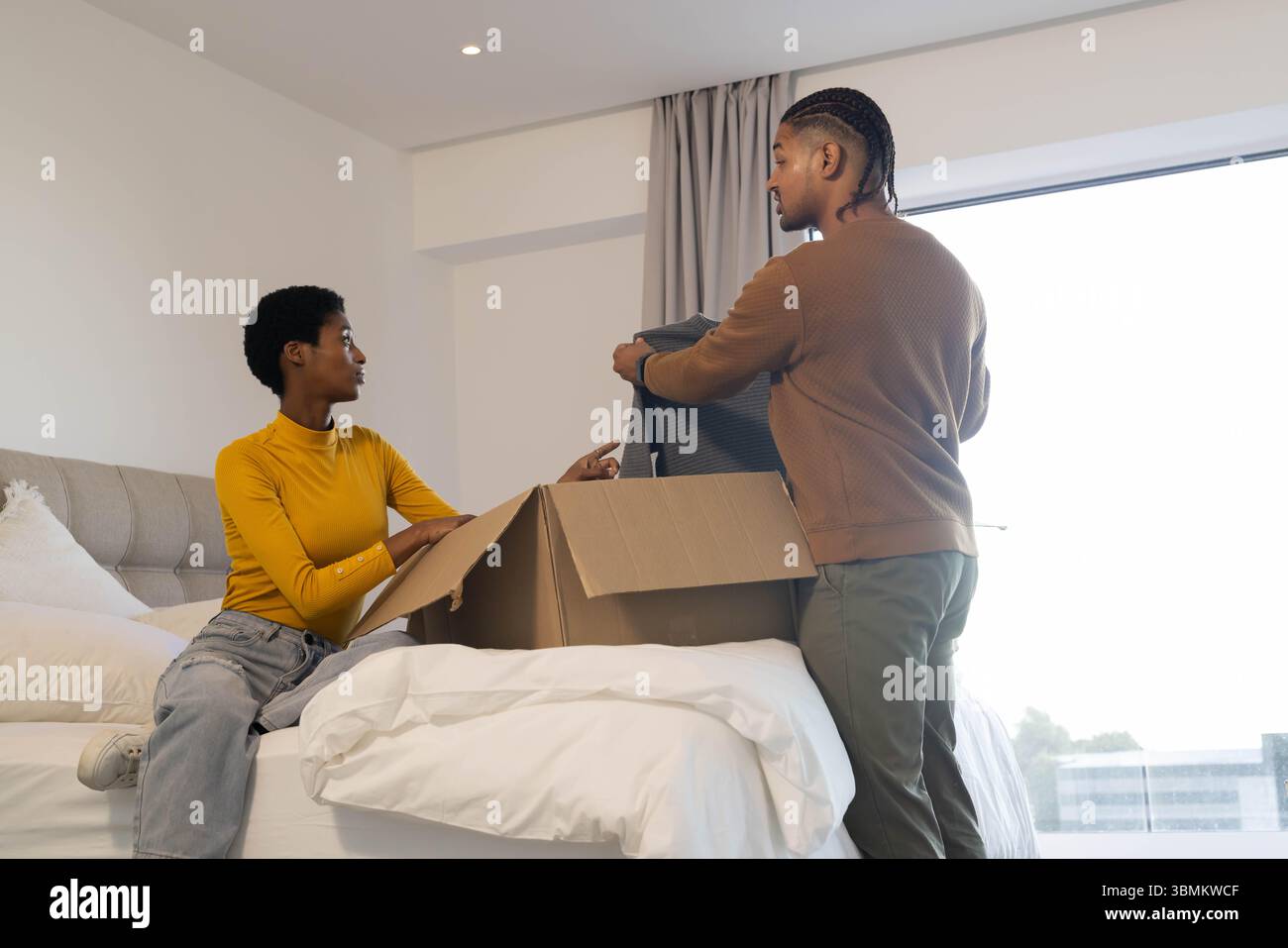 Unpacking Diverse couple sorting folded clothing on bed in apartment ...