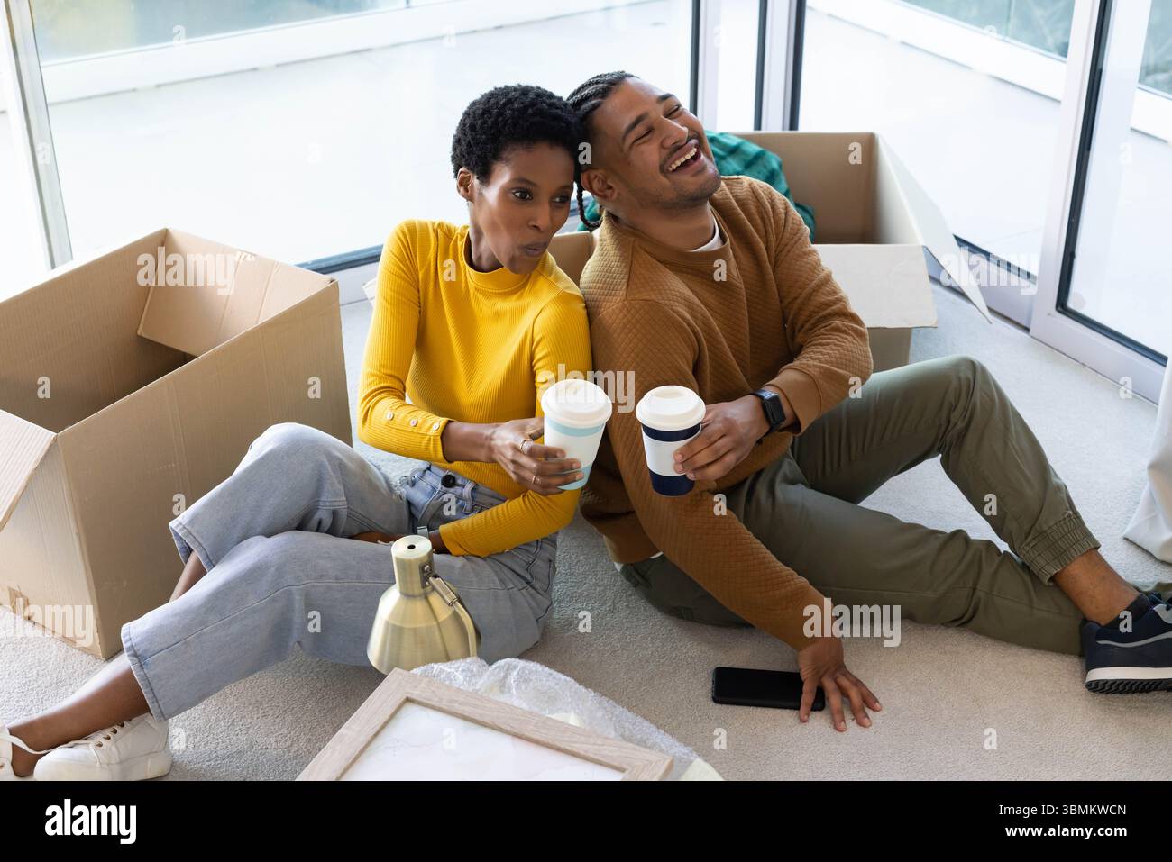 Leaning diverse couple unpacking boxes on living room floor, holding ...