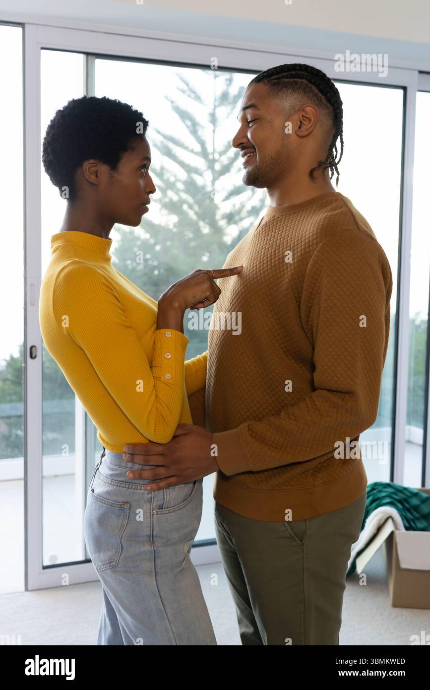 Diverse couple pointing at chest in room near glass doors, with cardboard box and teal blanket ...