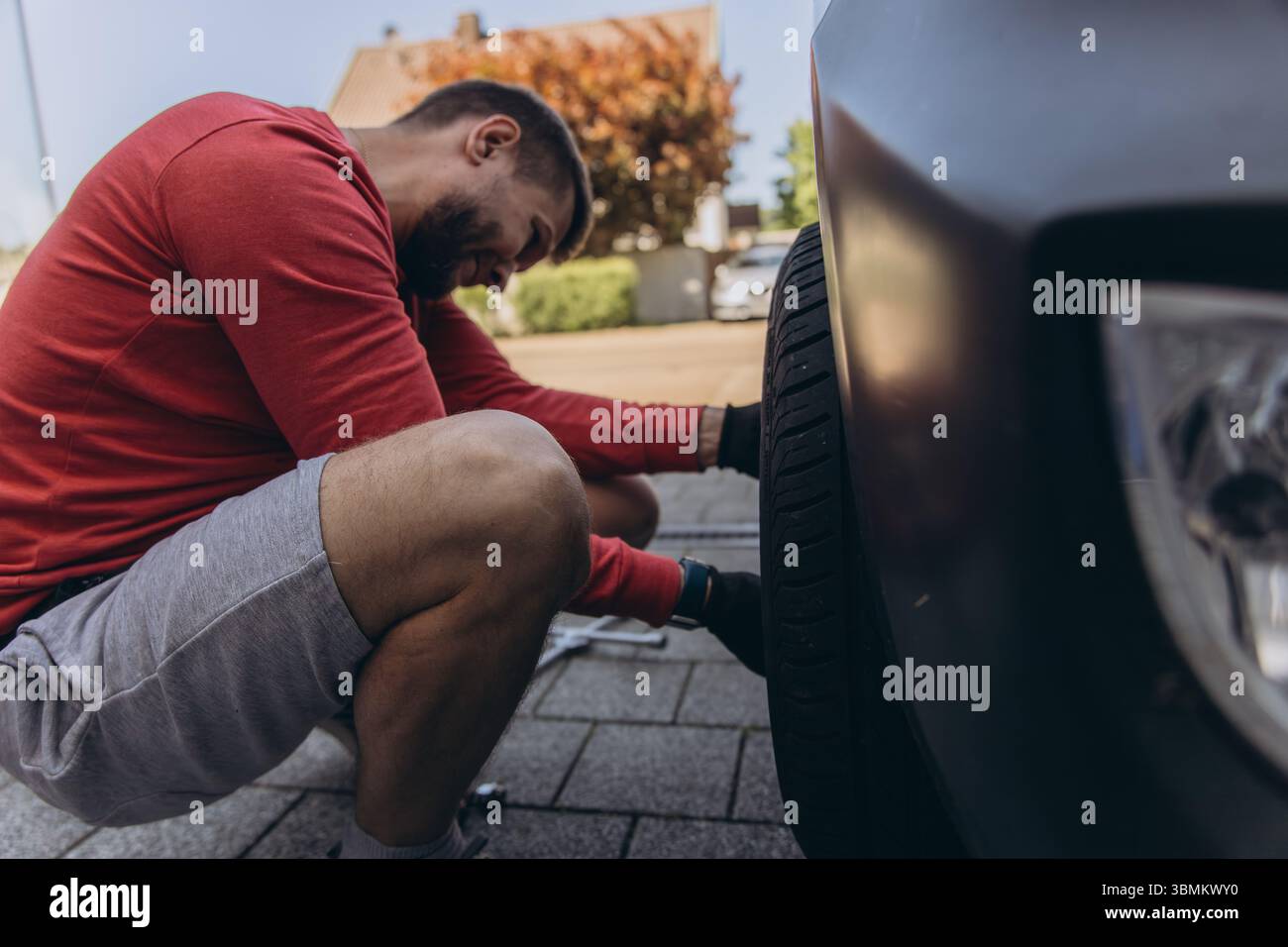 Man changing car tire on roadside using tools, vehicle lifted on jack ...