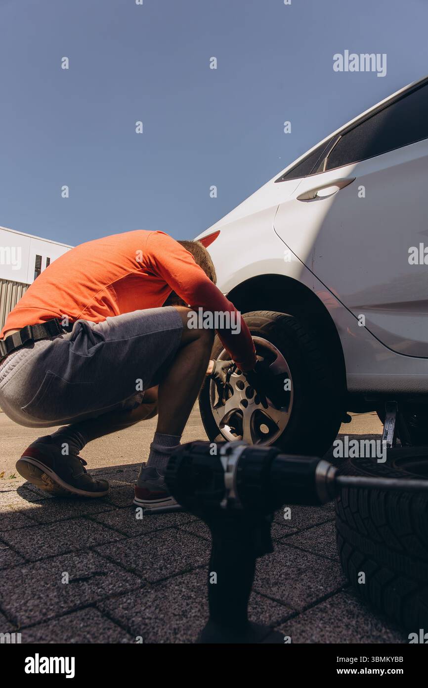 Man changing car tire on roadside using tools, vehicle lifted on jack ...