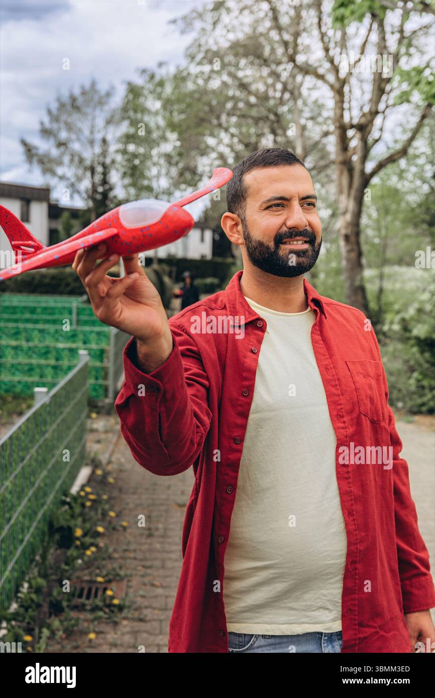 An Eastern man launching red toy airplane, enjoying playful and ...