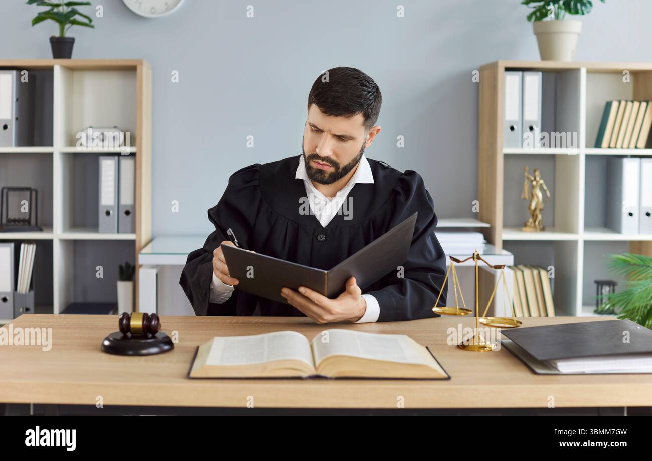 Man judge wearing judicial robe sitting at the desk with gavel and ...