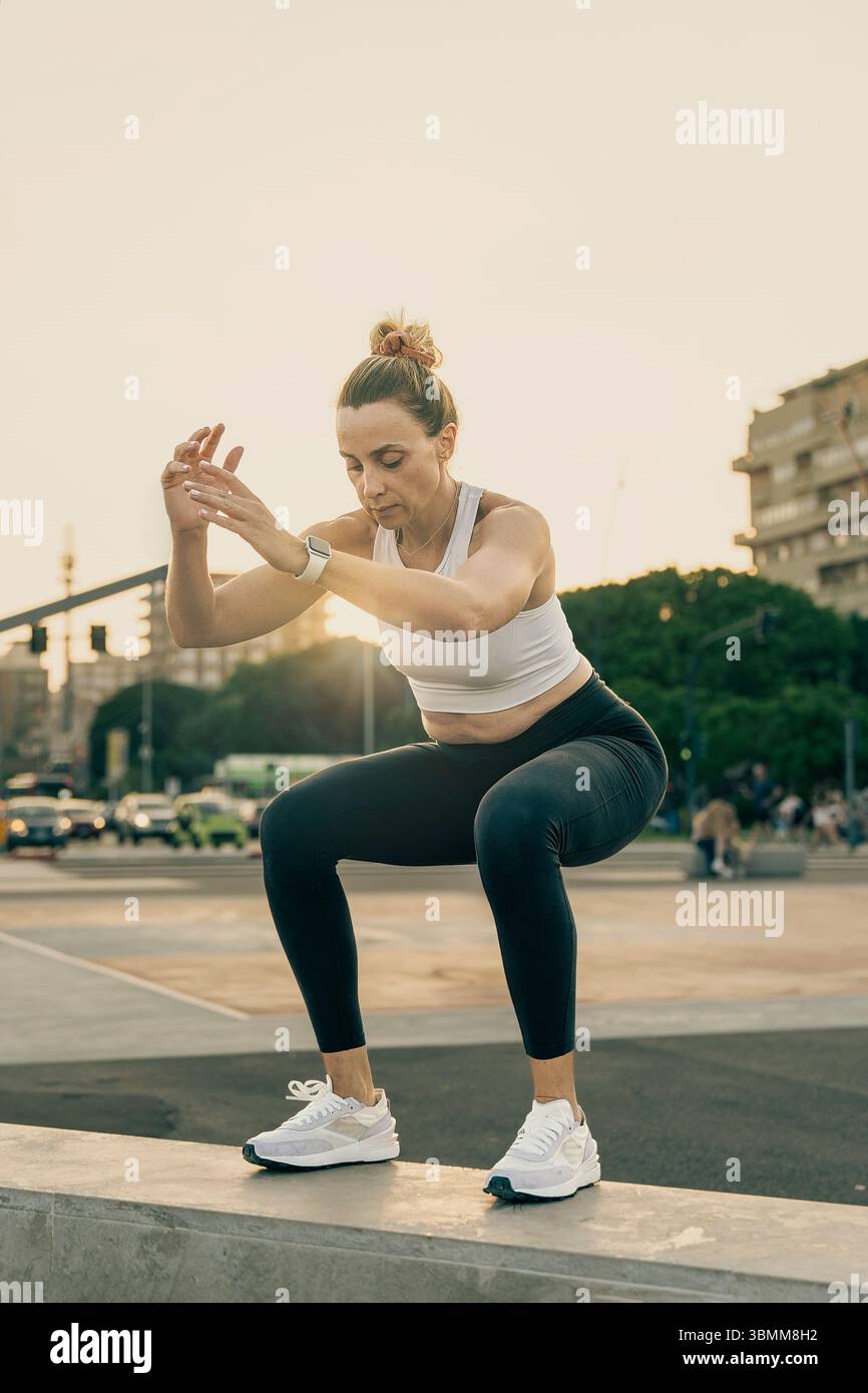 A strong woman lands a box jump, performing a squat as part of a ...
