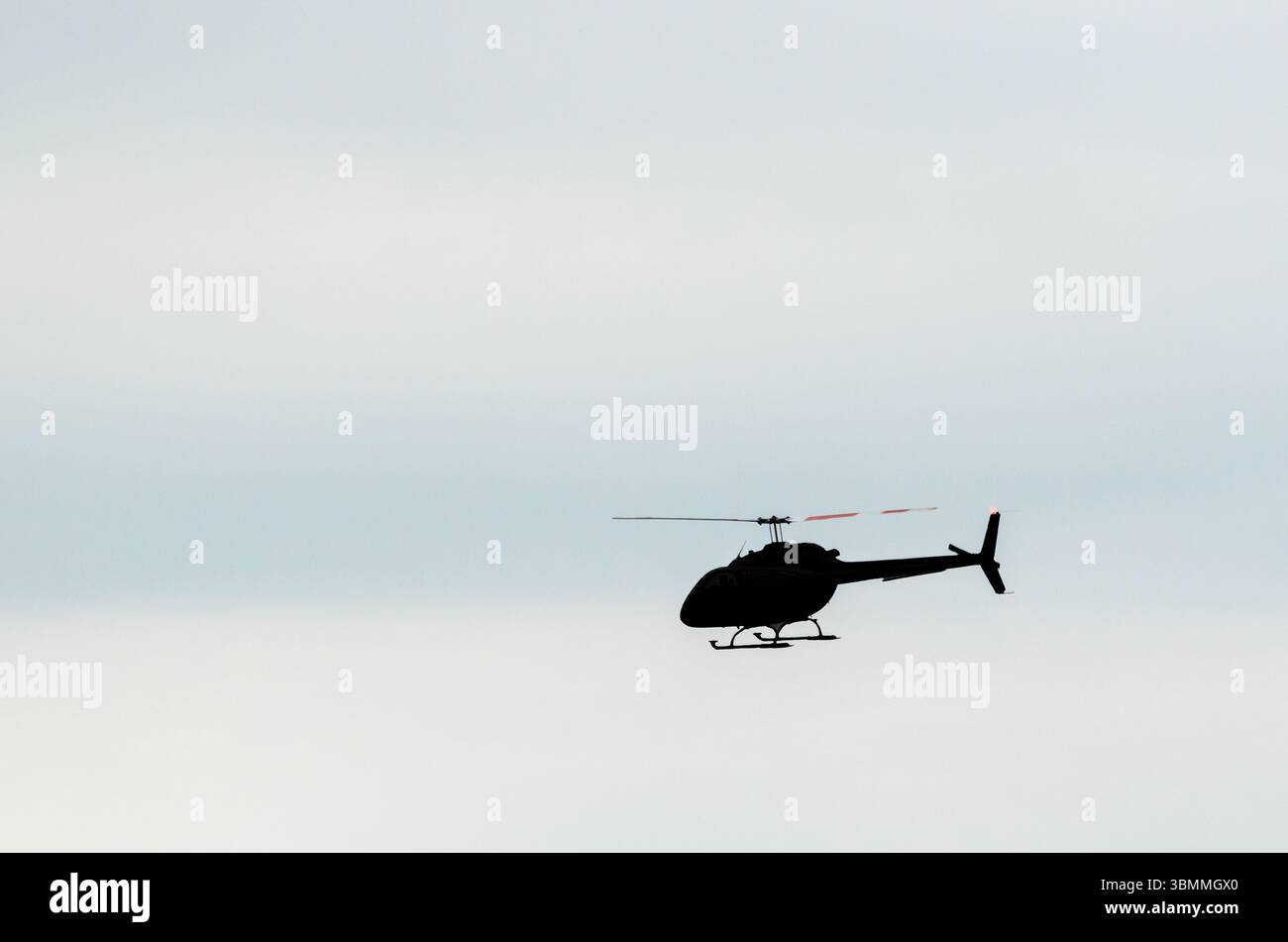 Single helicopter flying overhead silhouetted against a pale blue sky ...