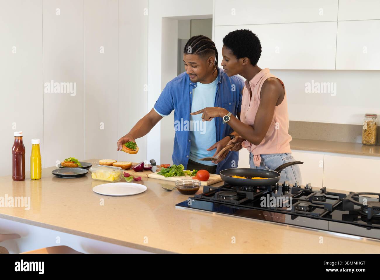Diverse couple assembling burger buns on kitchen counter, using lettuce ...