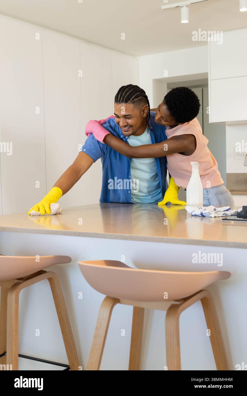 Hugging couple cleaning kitchen island at home, with yellow rubber ...
