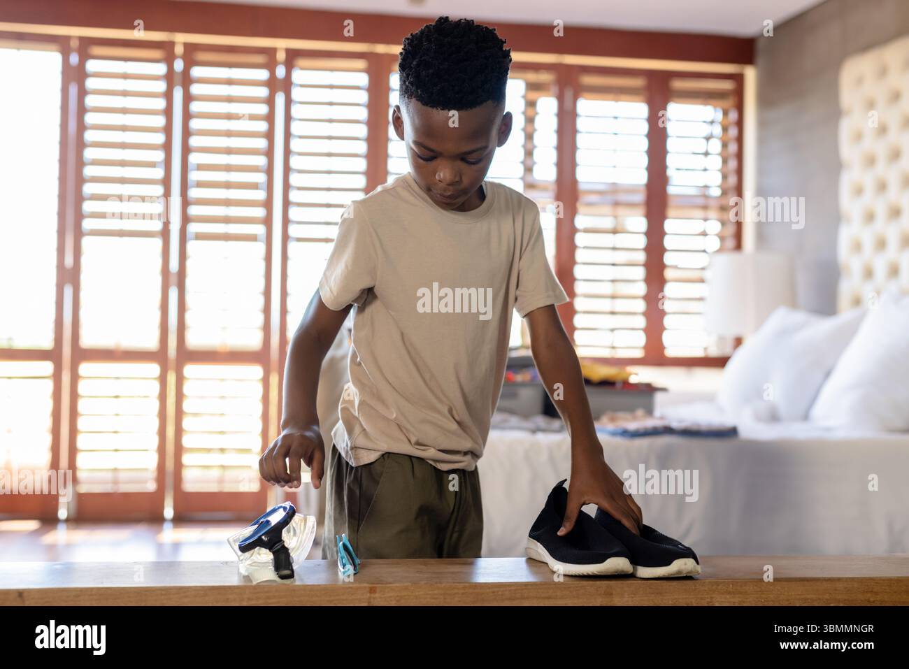 African American boy leaning over wooden bench picking up snorkel gear ...
