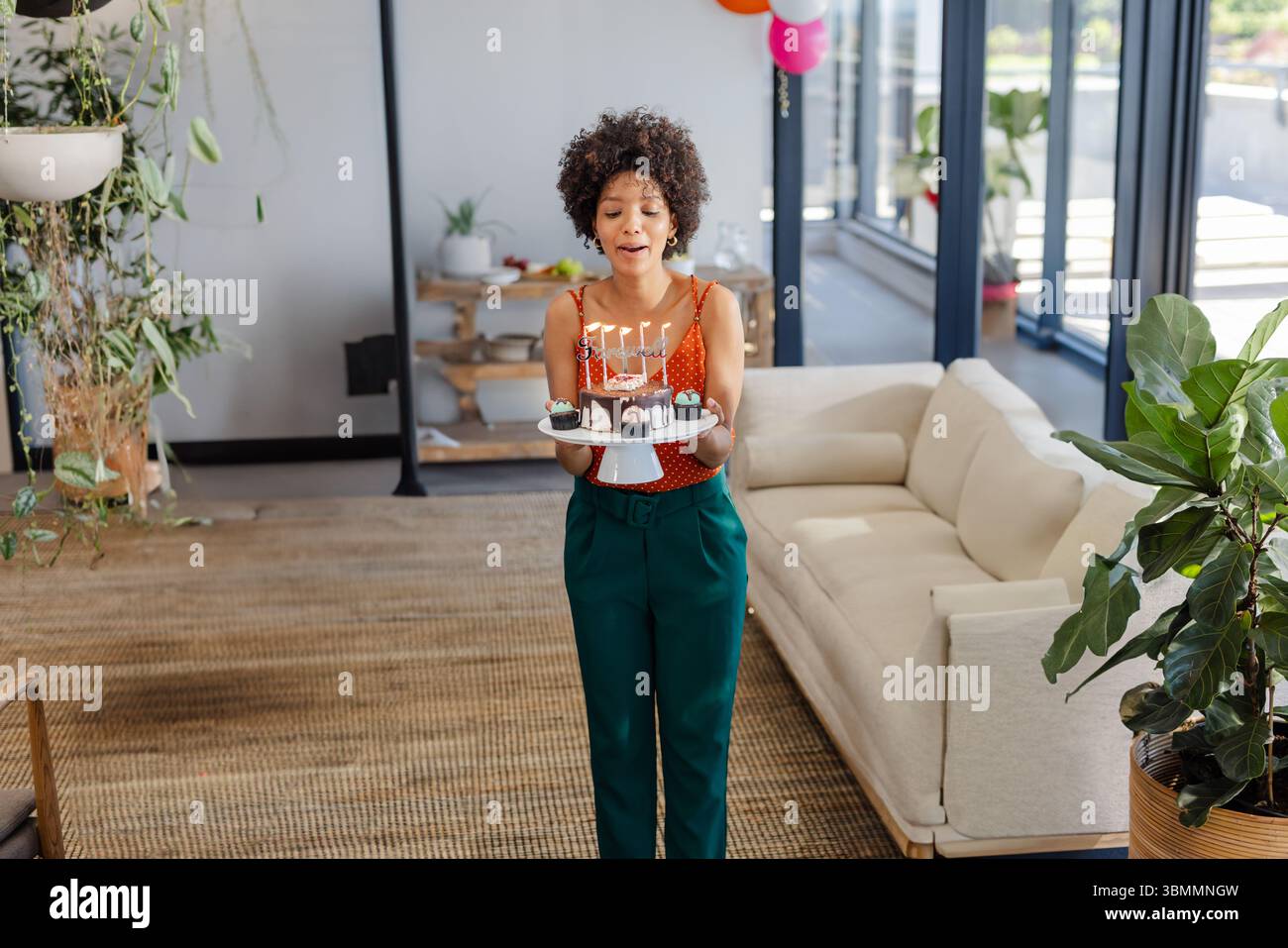 African American woman in red top holding cake stand with birthday cake ...