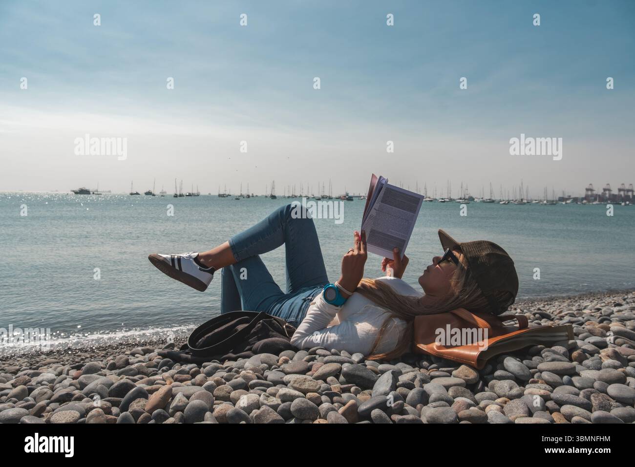 Student relaxing on a rocky beach reading a book enjoying summer ...