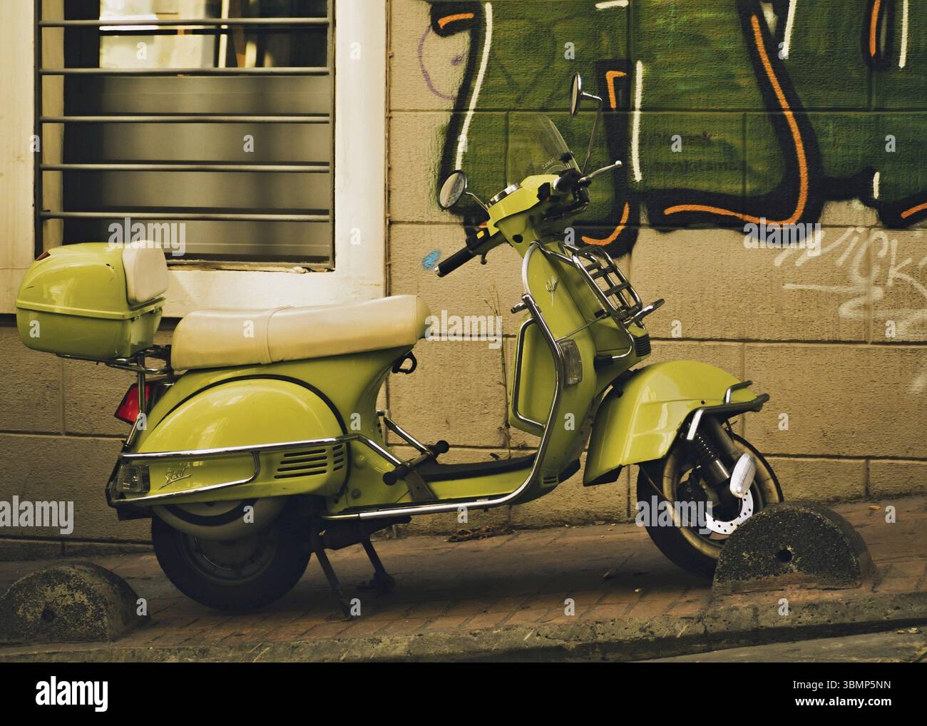 Classic scooter parked on a sidewalk near a graffiti wall, representing ...