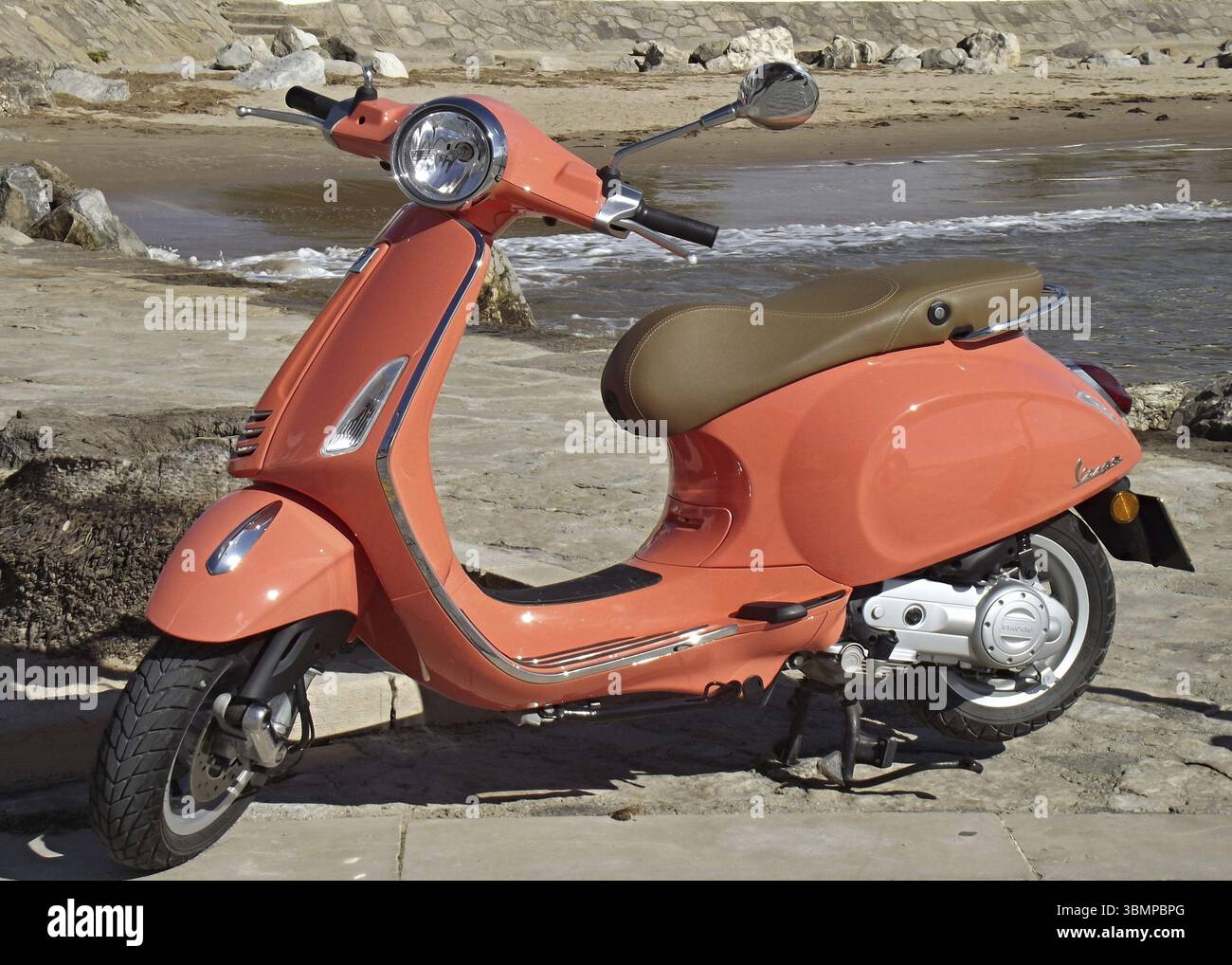 Shiny coral Vespa Primavera 50cc scooter parked on a pavement near a ...