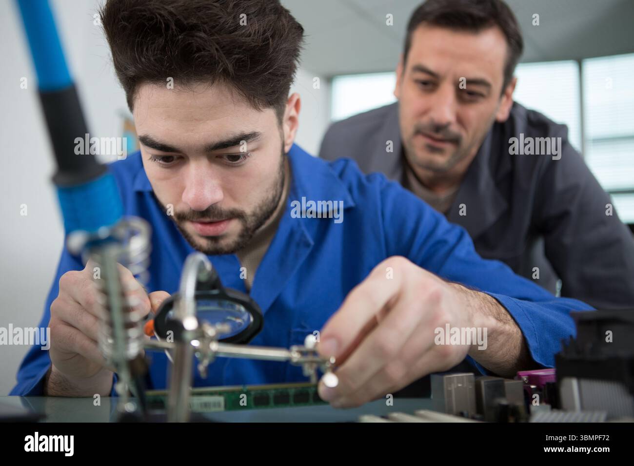 apprentice using magnifying glass to solder under supervision Stock ...