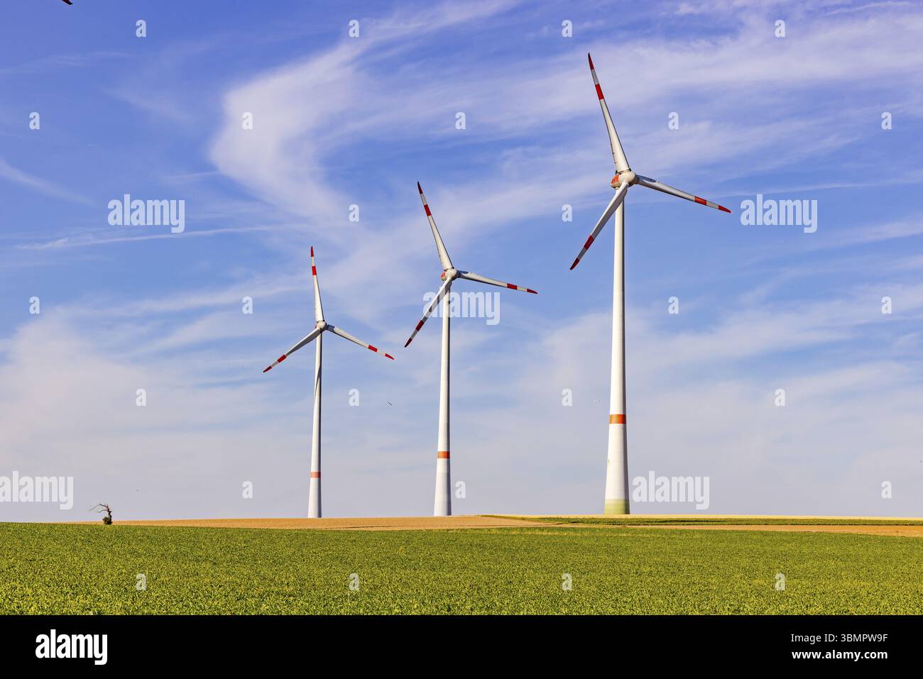 Three wind turbines of different sizes on an agricultural field next to ...