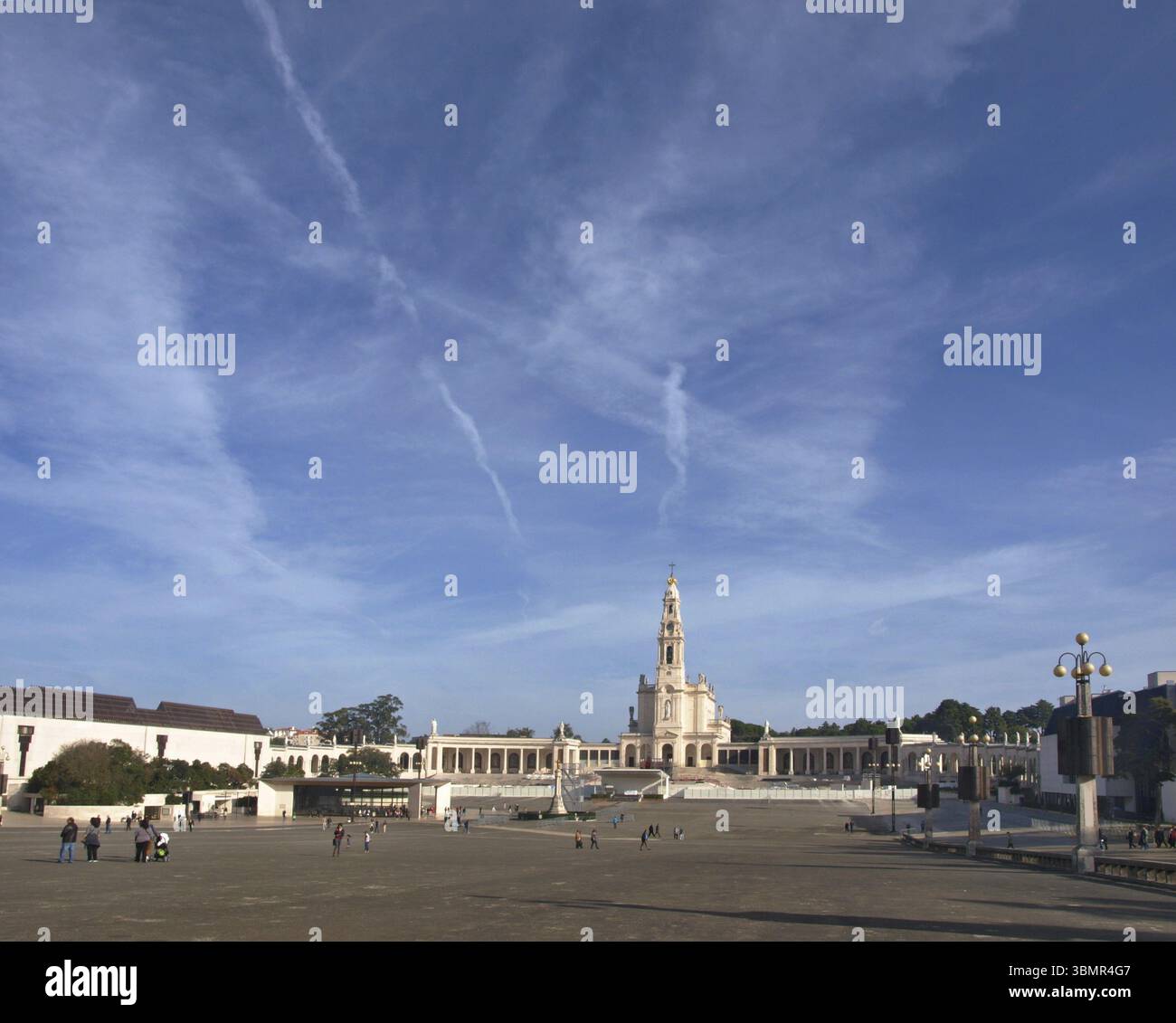 Tourists visiting the Sanctuary of Fatima under a blue sky with ...