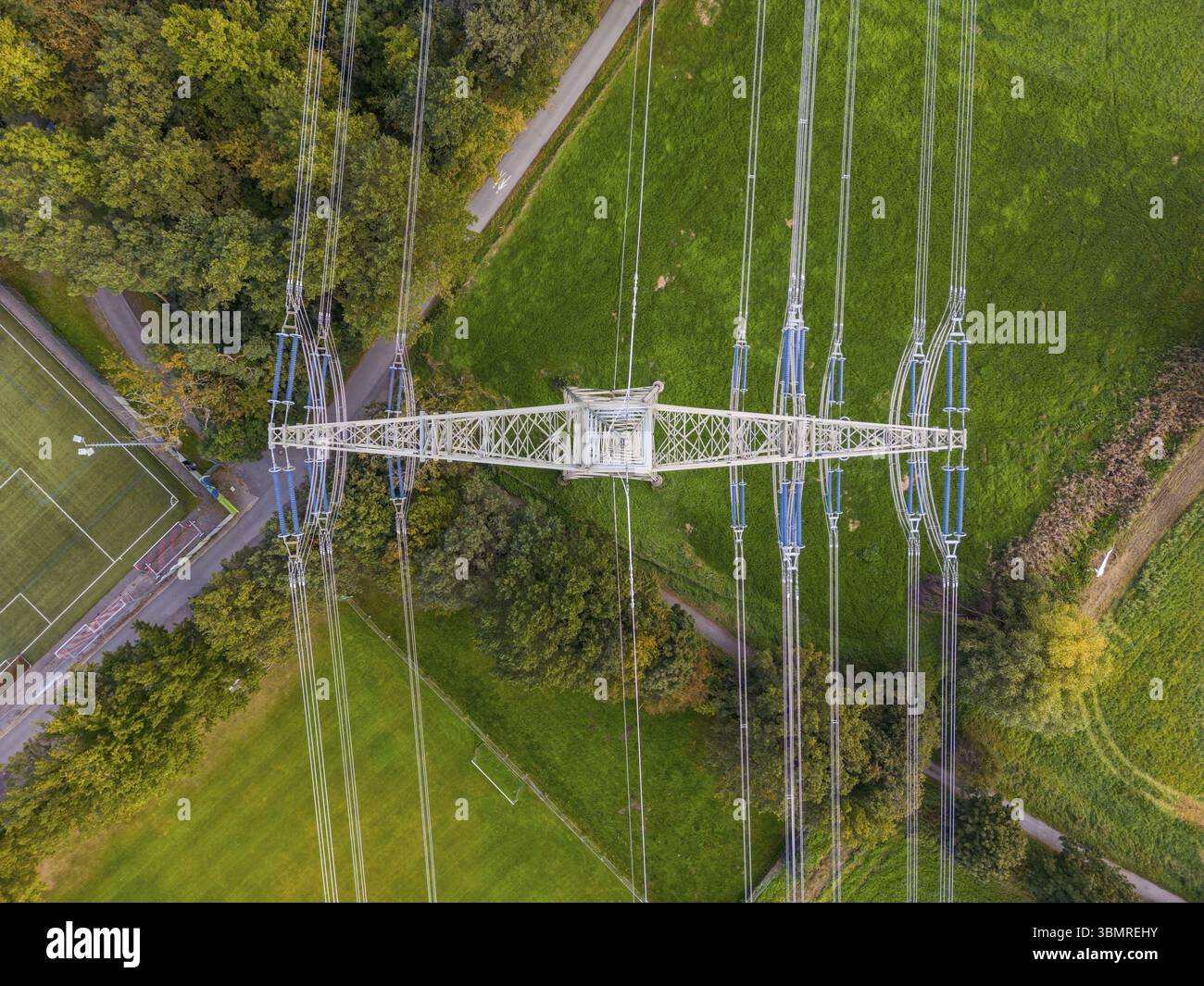 High voltage pylon with power lines between nature and sports field ...
