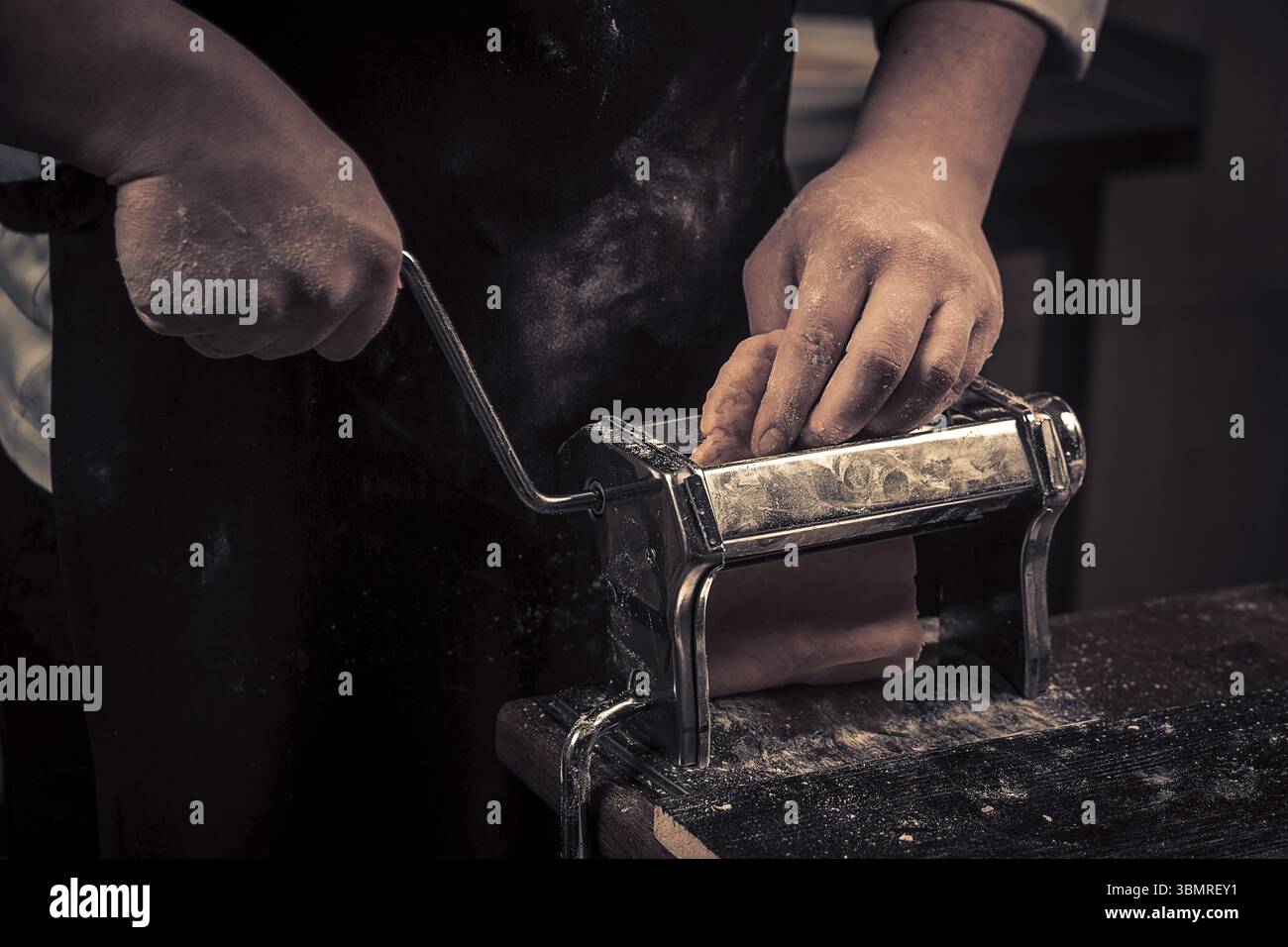 The chef makes fresh pasta from scratch. Wooden table. Photo in brown ...