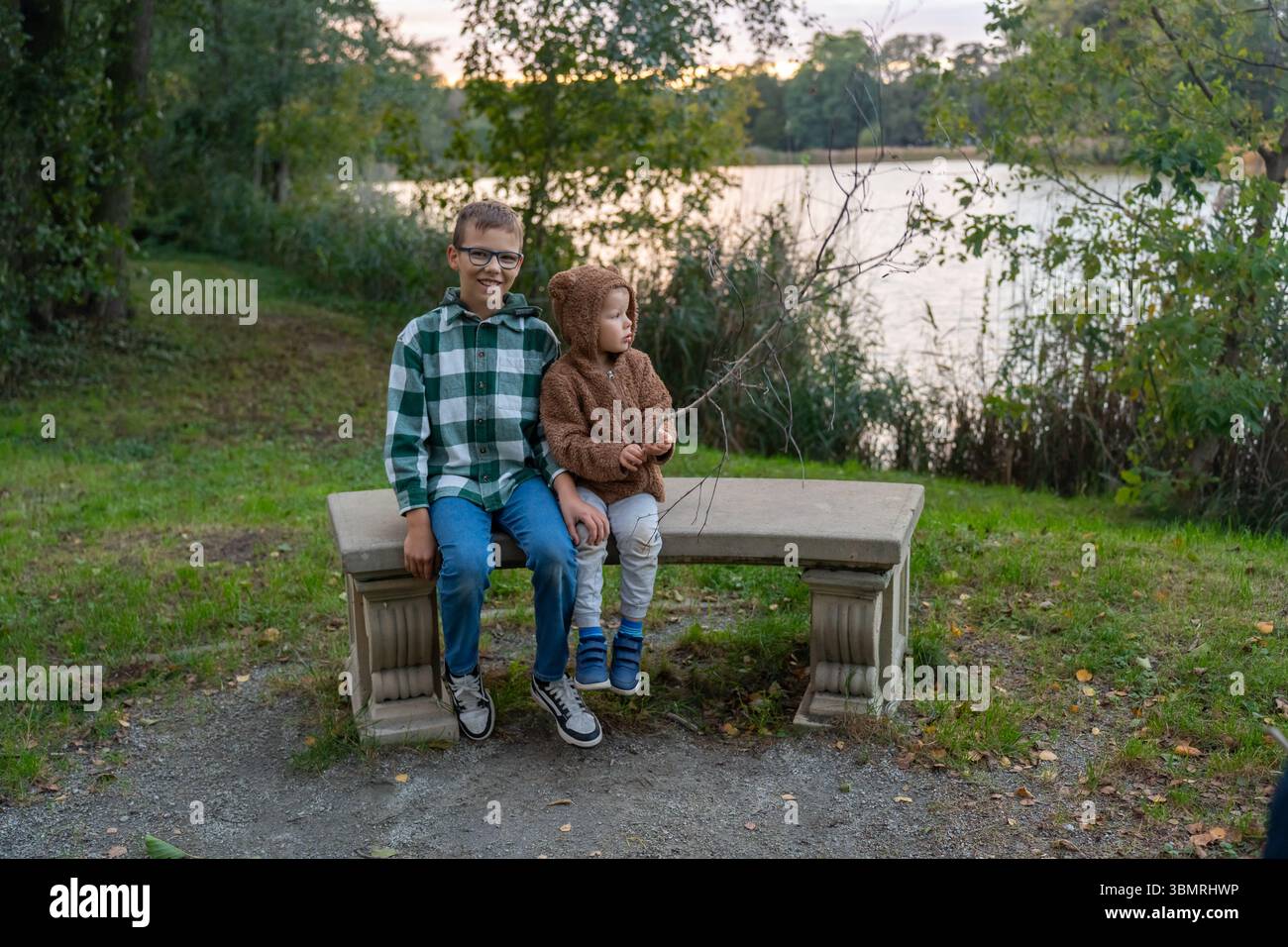 Two happy brothers sitting on stone bench in autumn park near lake ...