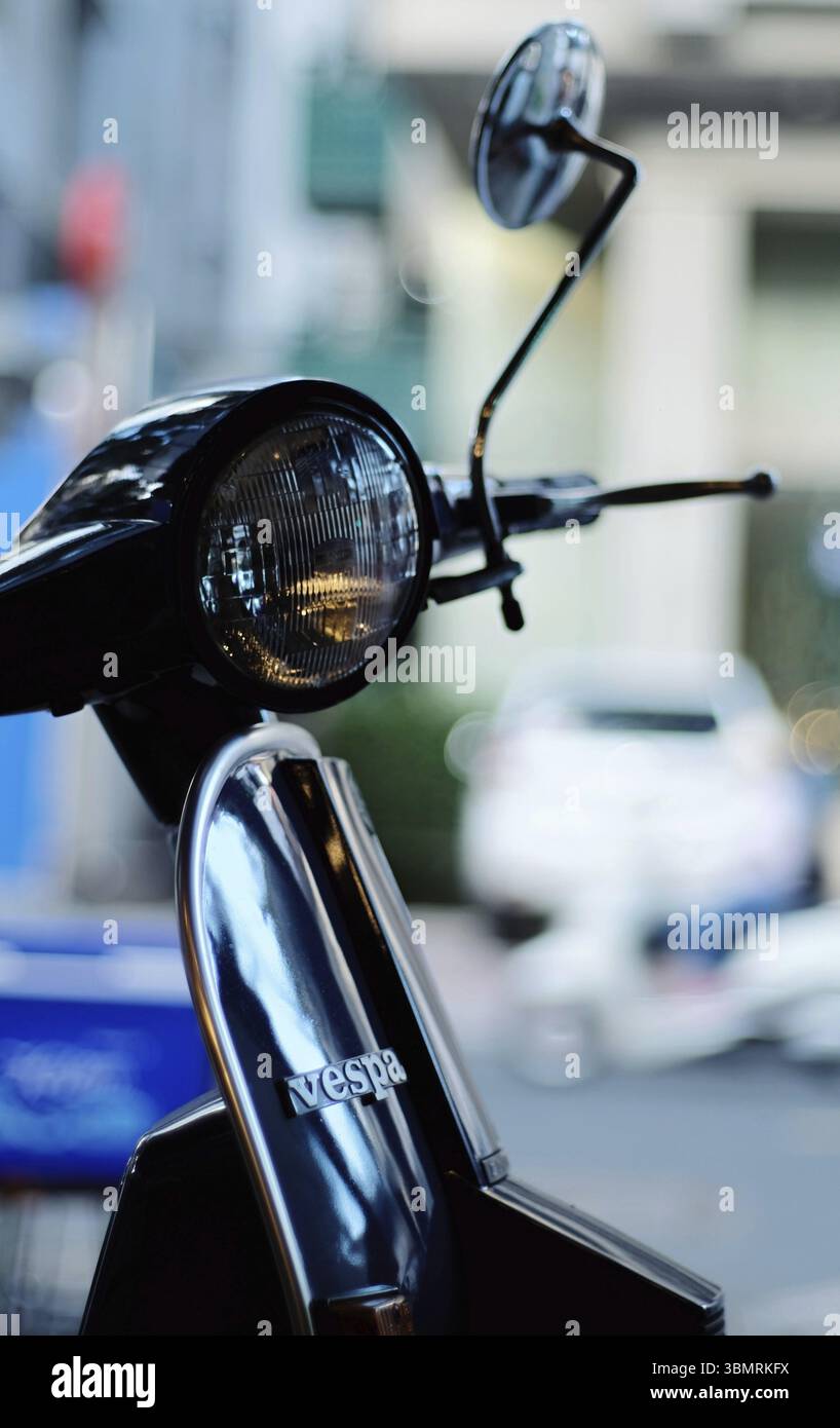 Shiny black Vespa scooter parked on a blurred urban street, showcasing ...