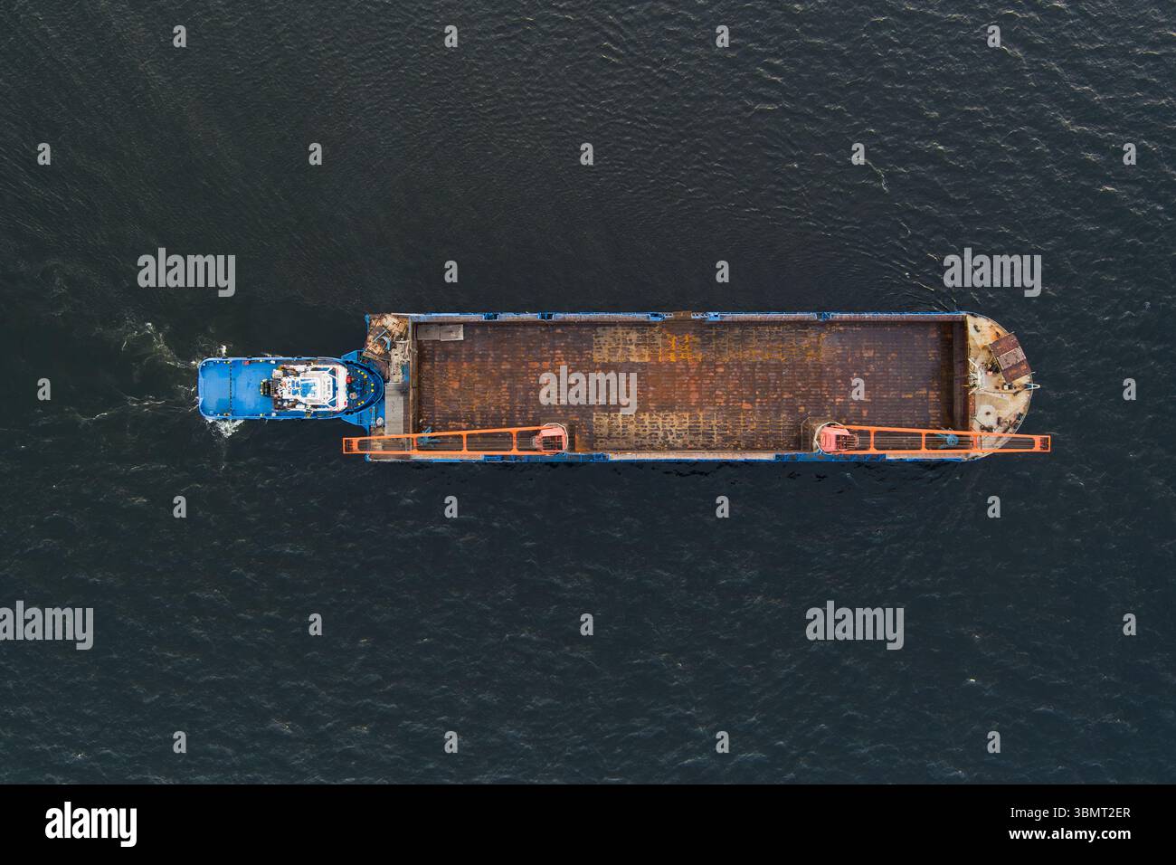 Drone view of a powerful tugboat pushing a large empty barge with a ...