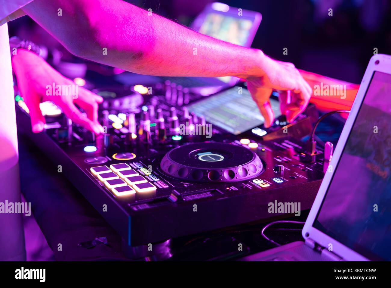 DJ music console and laptops in bright colors of light in night club ...