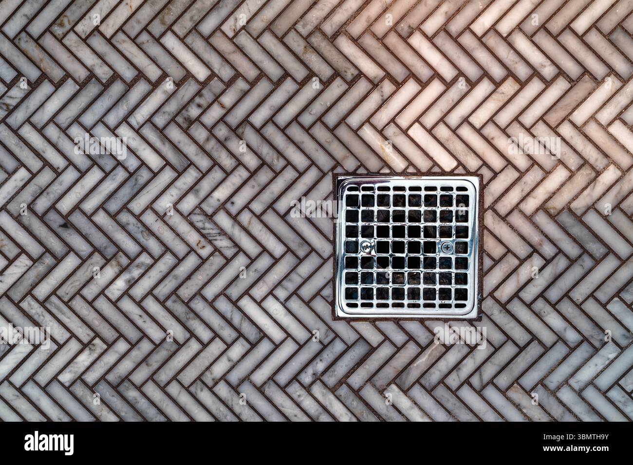 A shiny metal shower drain with diagonal herringbone style tiles Stock ...