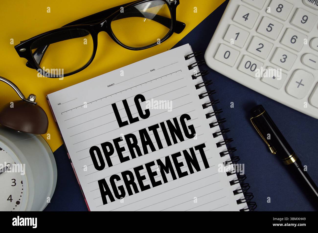 LLC Operating Agreement text written on notepad with calculator and alarm clock on navy blue ...