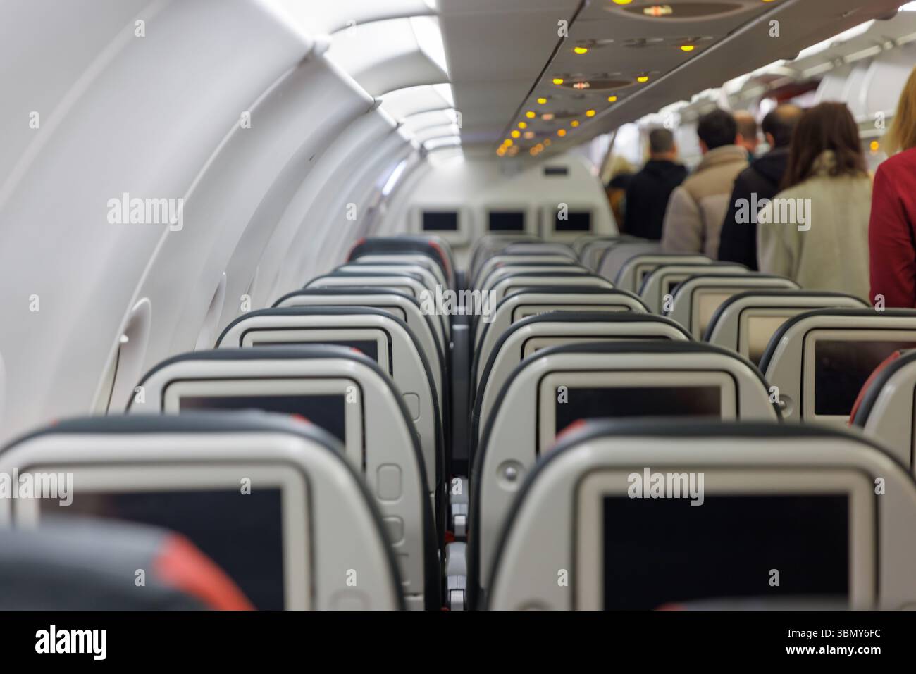 A crowded airport terminal shows passengers lining up to board a plane. The interior features ...