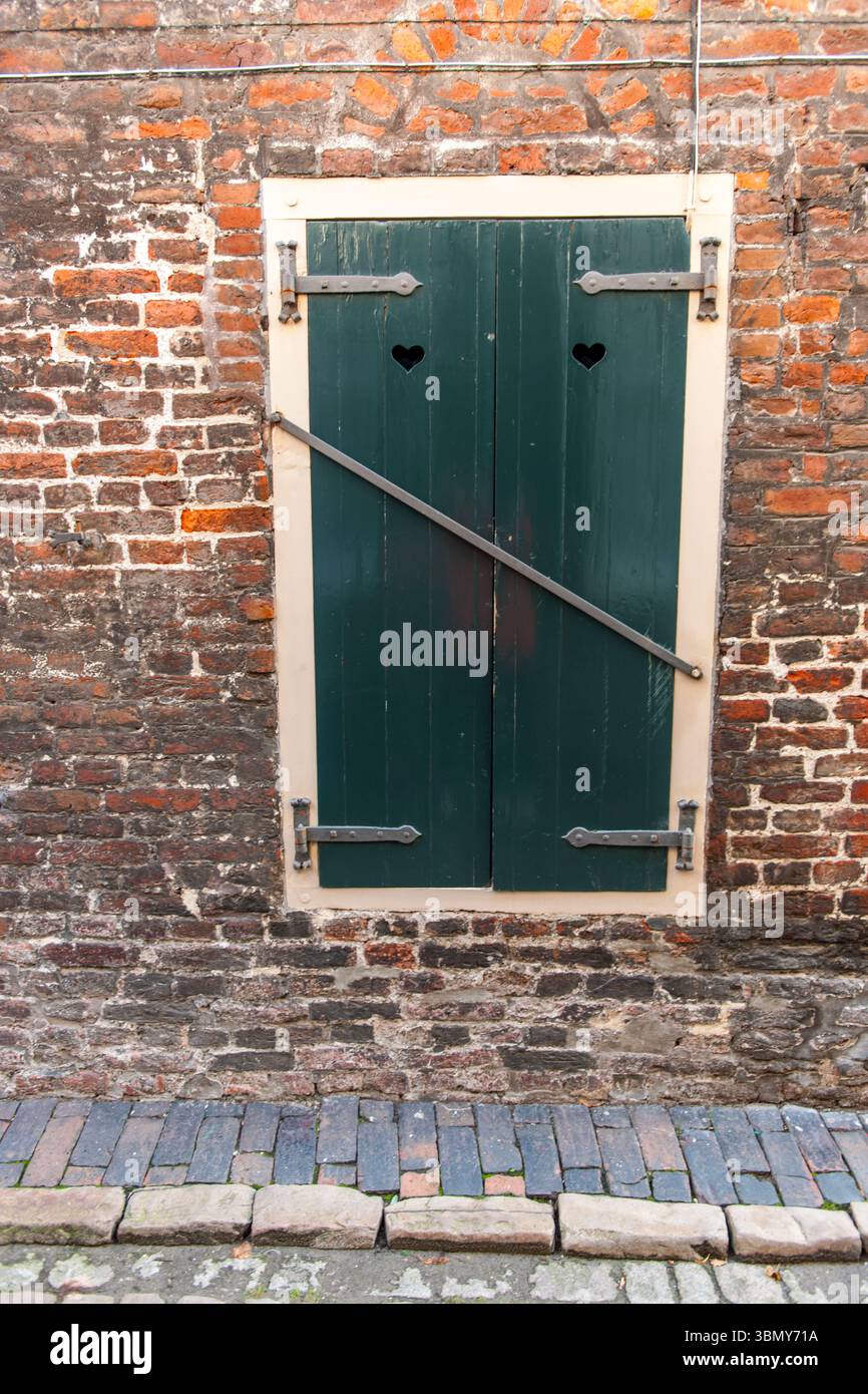 Frontal view of an old window with locked shutters in a weathered brick ...
