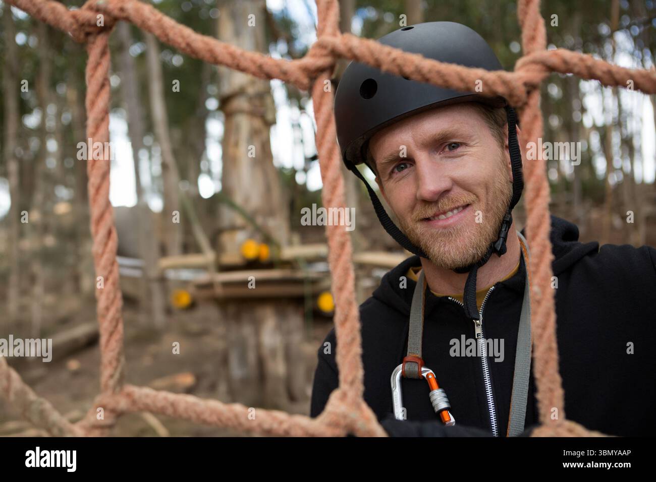 Man standing on platform behind rope net in forest course wearing ...