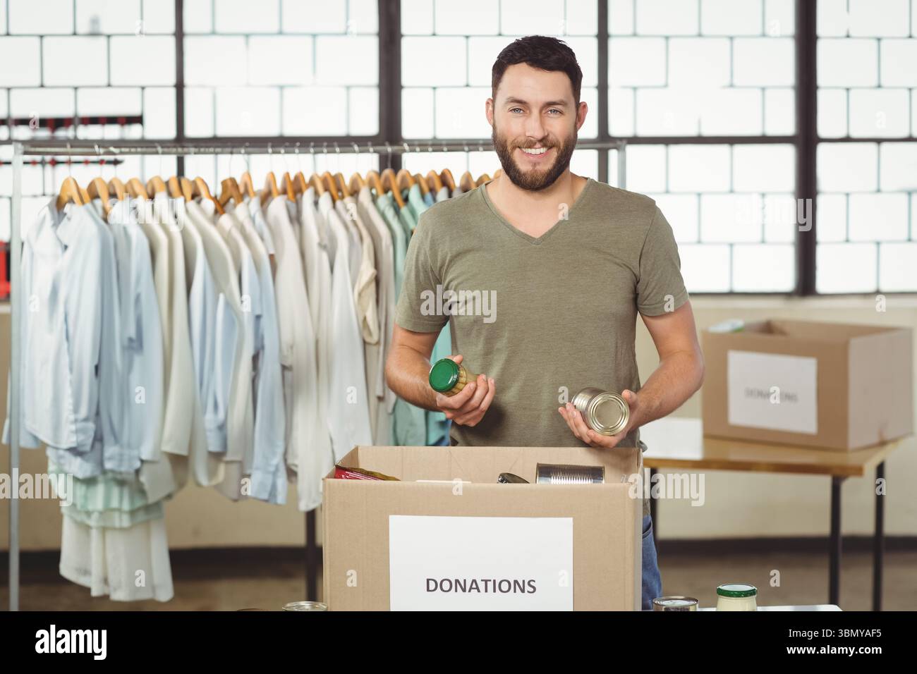 Volunteer man sorting canned food inside donation center by clothing ...