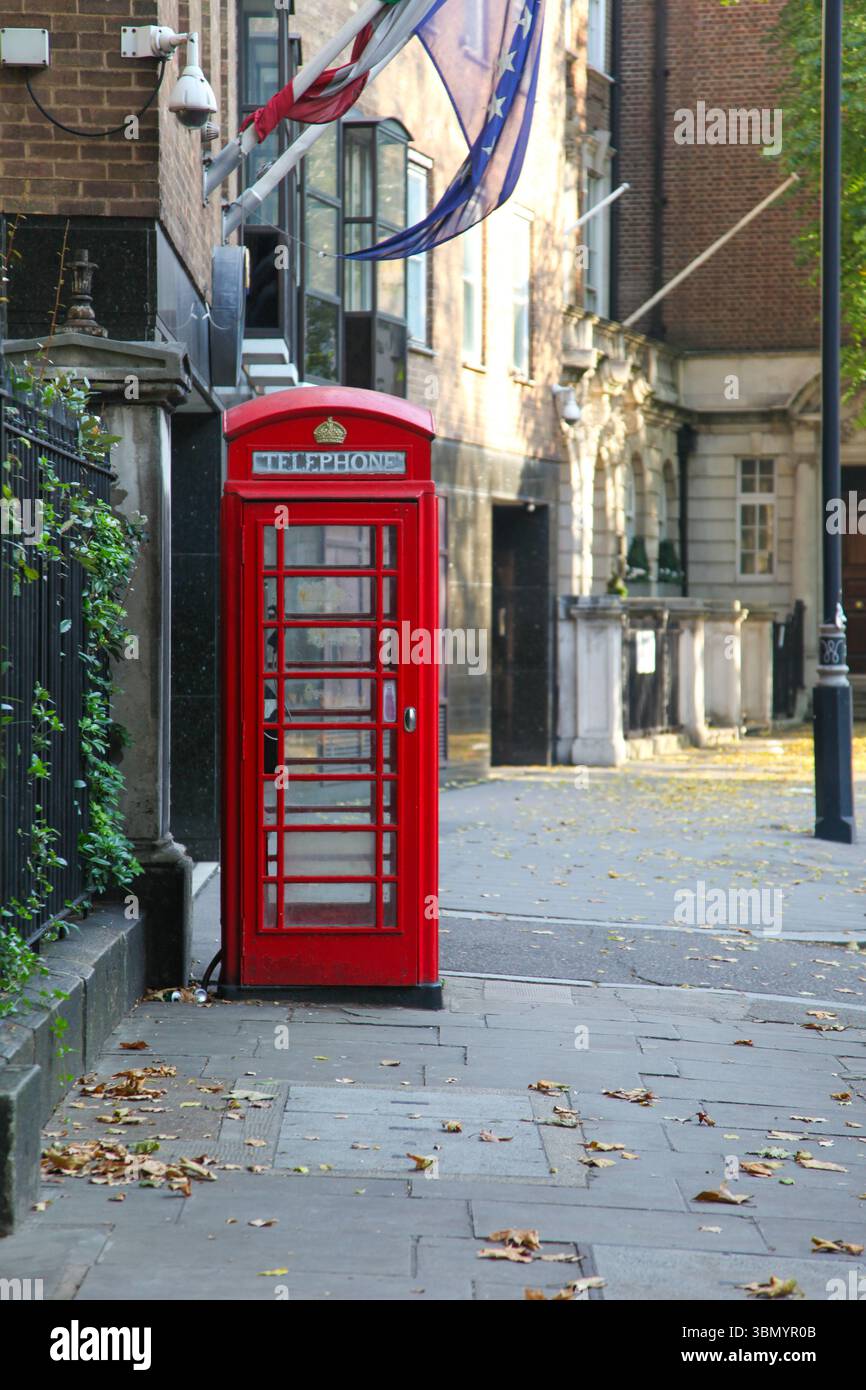 Traditional red phone booth in London with autumn leaves on the ground ...