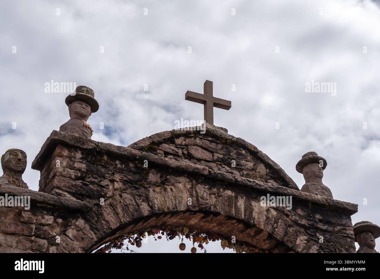 A stone arch with a cross and carved figures marks an entrance in a ...